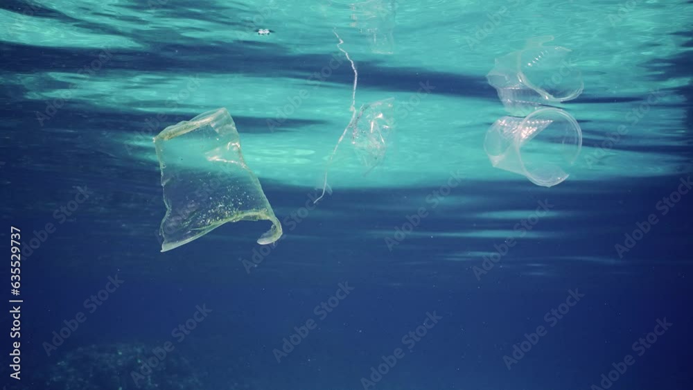 Close-up of plastic debris drifts under surface in blue water, Slow ...