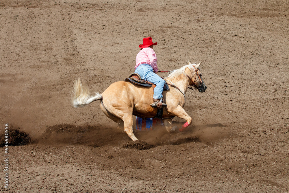 Cowgirl riding in a barrel racing completion at a rodeo. She is wearing ...