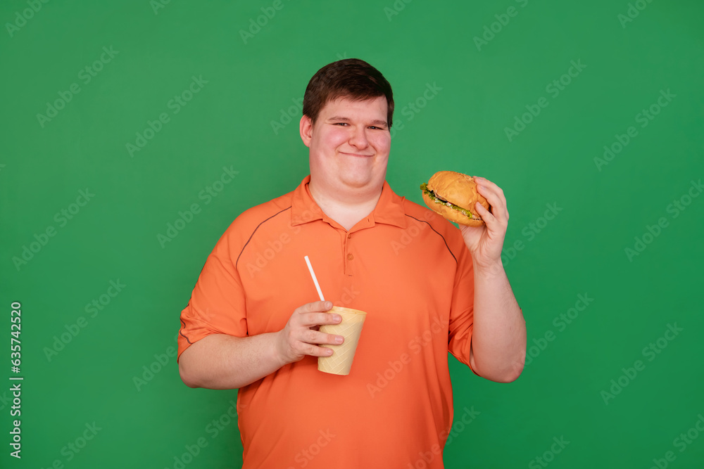 Portrait of a fat guy eating a big hamburger and drinking soda from a ...