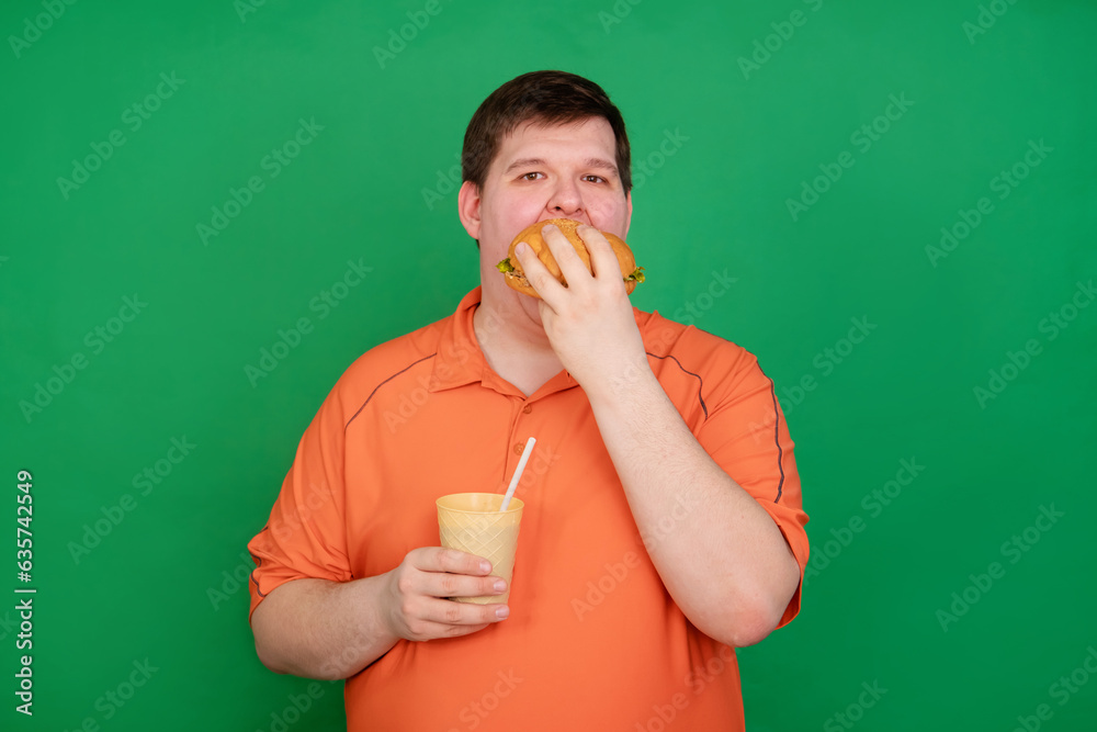 Portrait of a fat guy eating a big hamburger and drinking soda from a ...