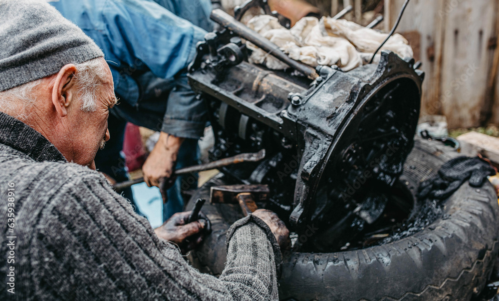 elderly man tuning a car engine at home in a garage, customizing an ...