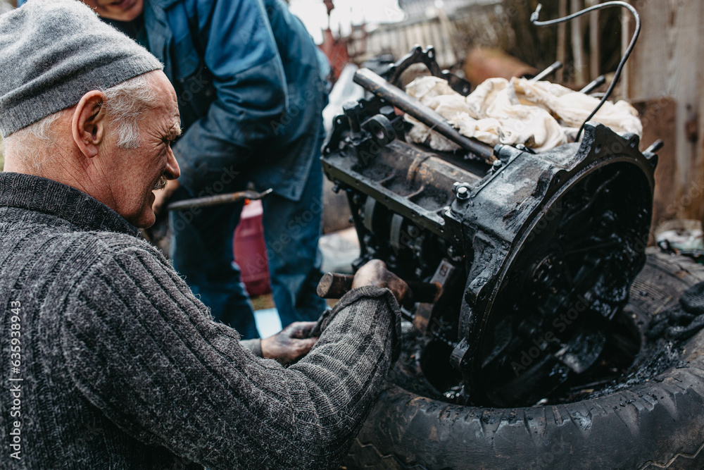 elderly man tuning a car engine at home in a garage, customizing an ...