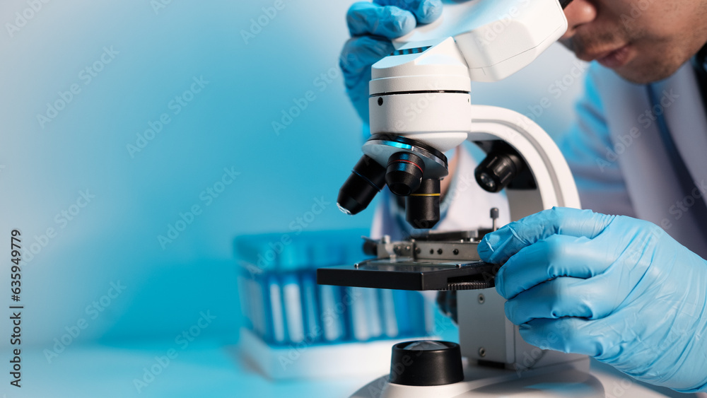 male medical scientist examining specimen using microscope in modern ...