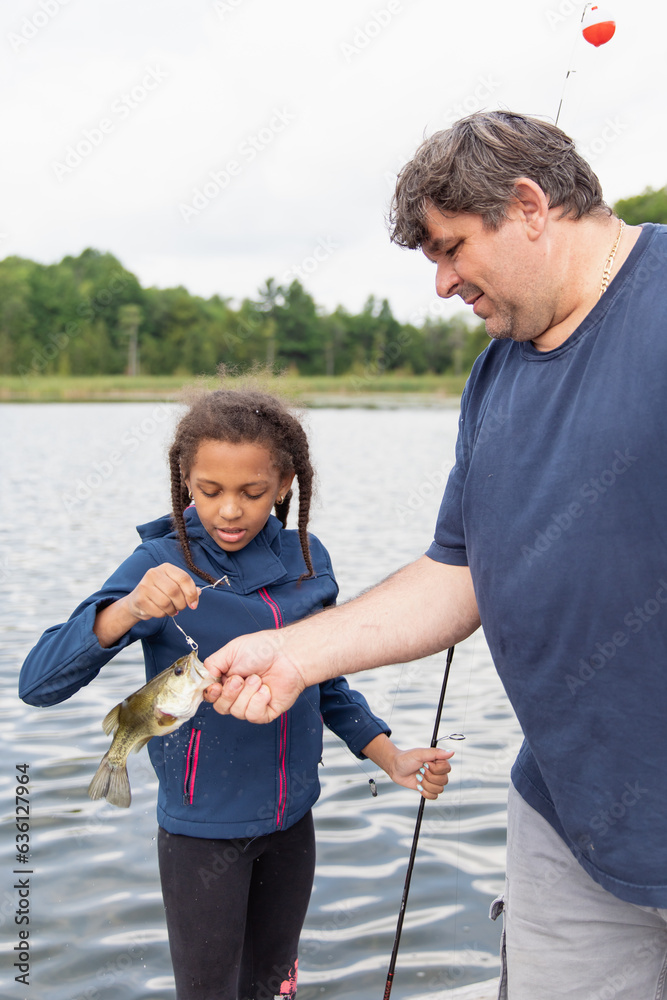 Father helping his child to remove a caught fish from her fishing hook ...