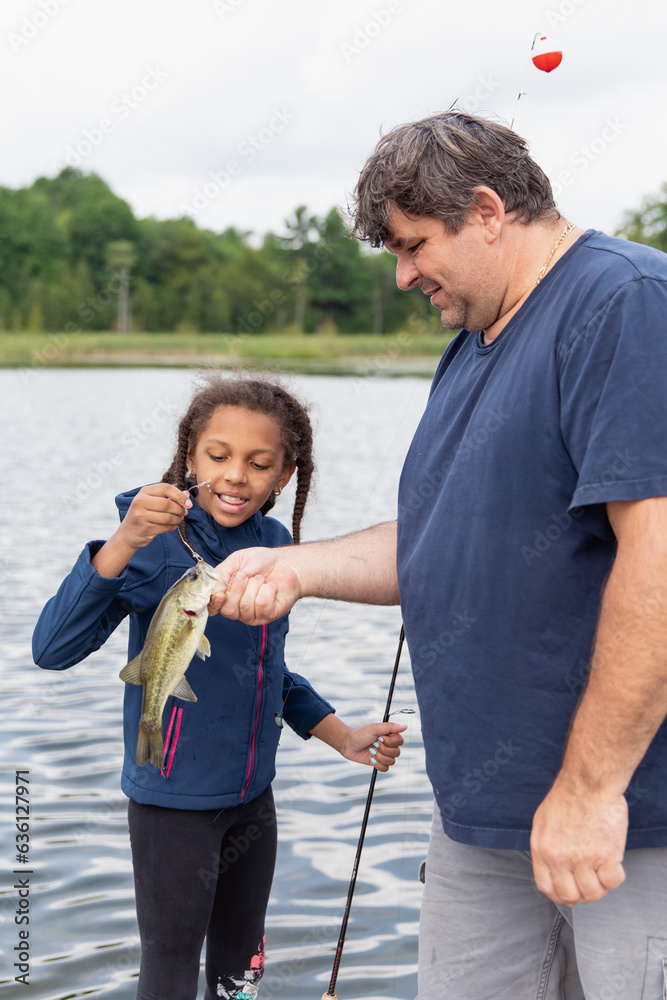 Father helping his child to remove a caught fish from her fishing hook ...