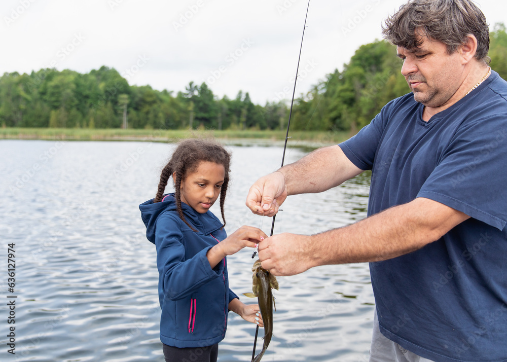 Father helping his child to remove a caught fish from her fishing hook ...