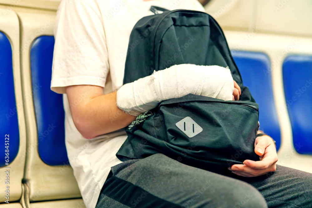 A man with a broken arm in a cast rides the subway and holds a backpack ...