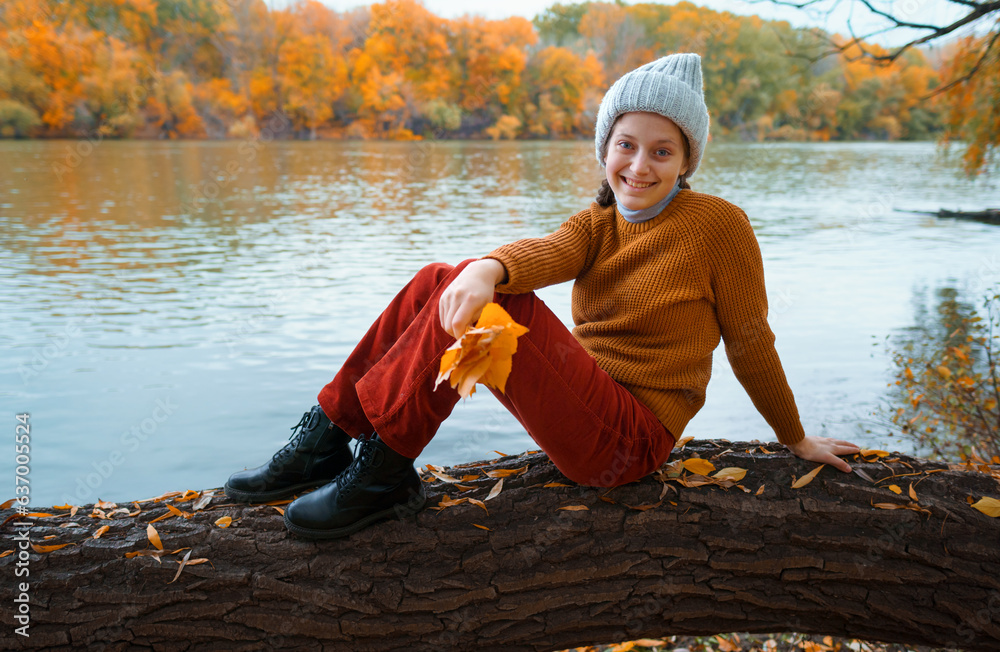 a young teenage girl posing in an autumn forest, sitting on a tree by ...