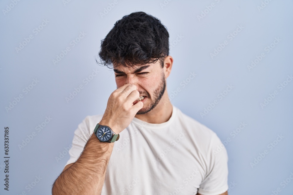 Hispanic man with beard standing over white background smelling ...