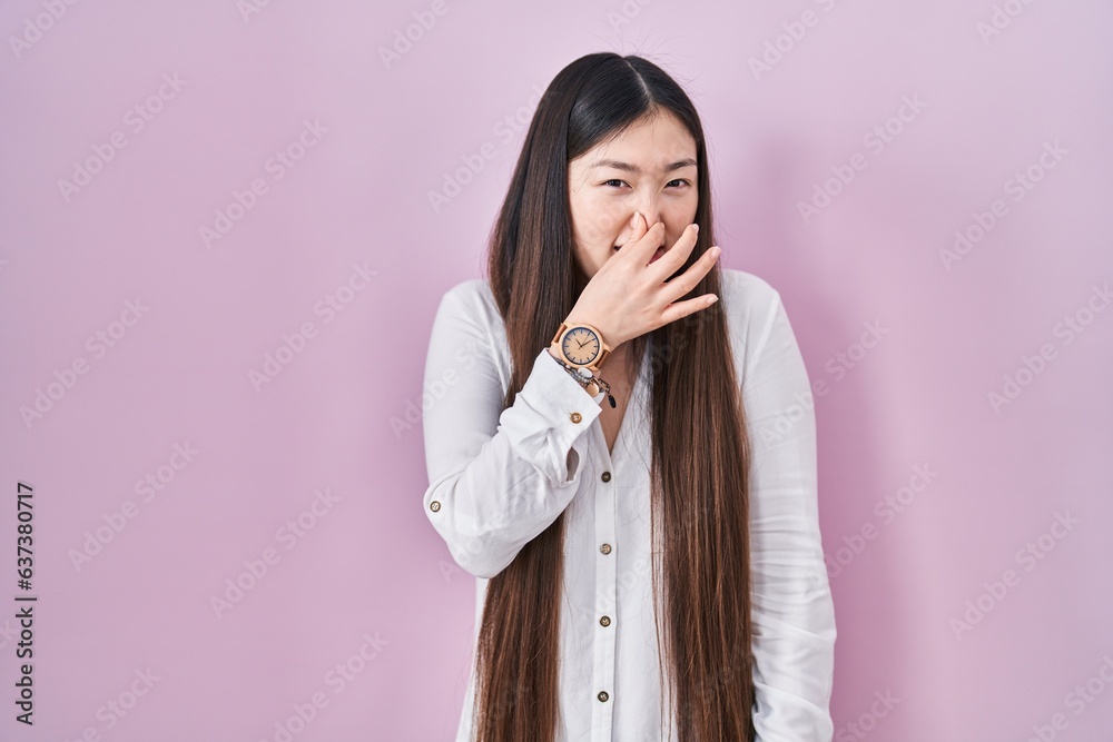 Chinese young woman standing over pink background smelling something ...
