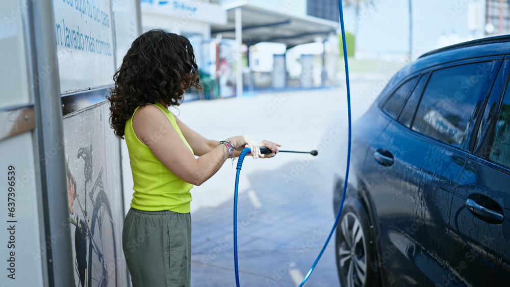 Middle age hispanic woman washing car with pressure washer at car wash ...
