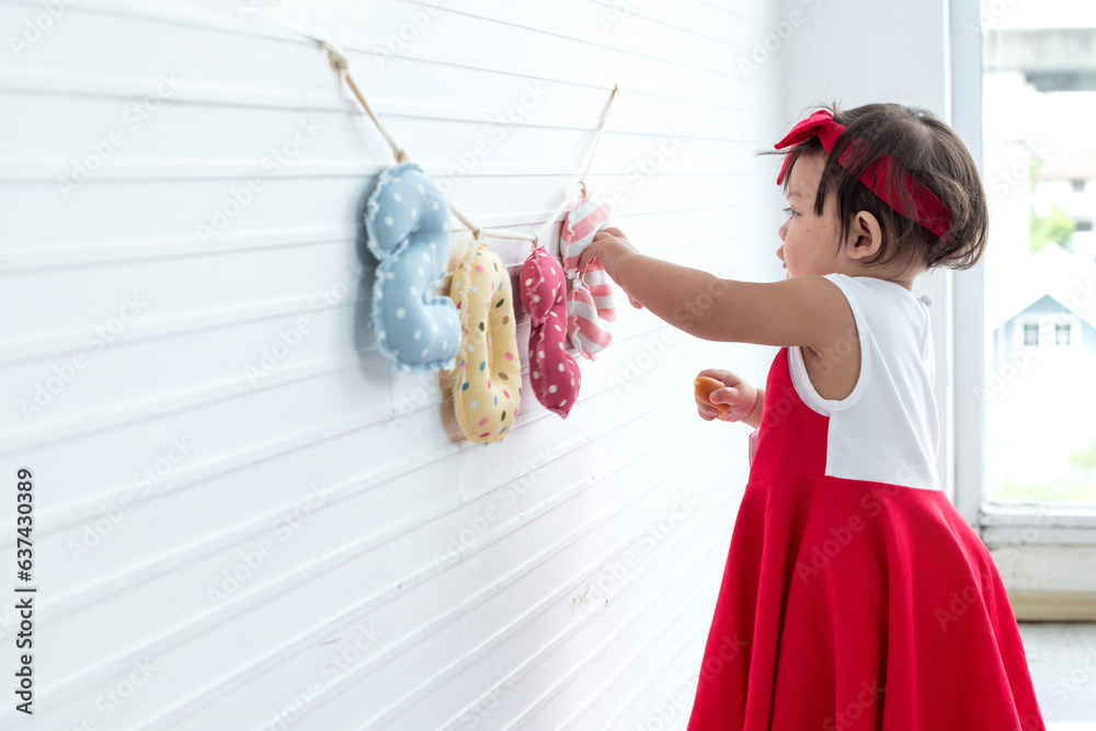 Cute little girl in red dress interested with numbers hanging on string ...