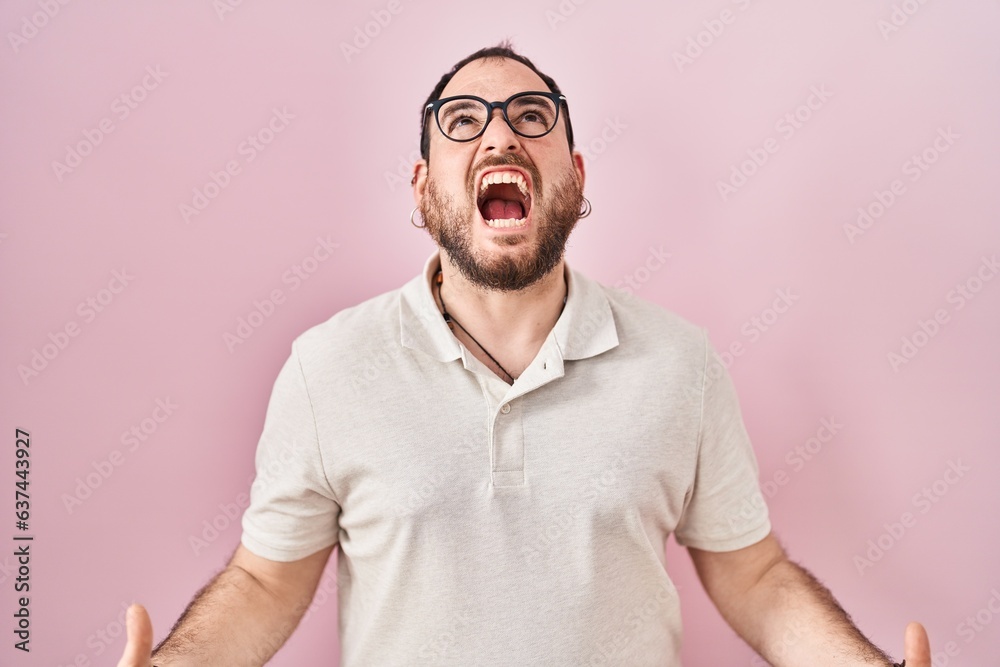 Plus size hispanic man with beard standing over pink background angry ...
