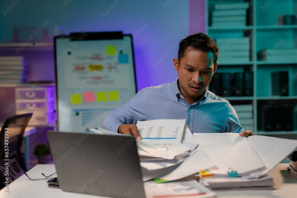 Serious young Asian male worker working alone with computer and ...