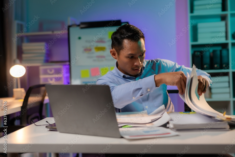Serious young Asian male worker working alone with computer and ...