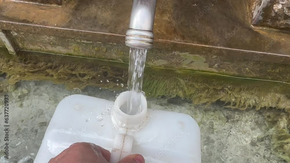 Filling a white canister with fresh, cold, clean water flowing from a ...