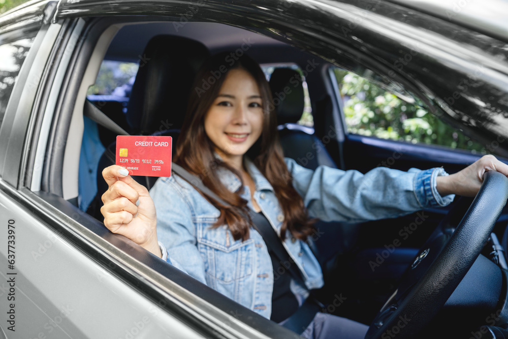 Pretty happy asian woman sitting in new car and showing credit card ...