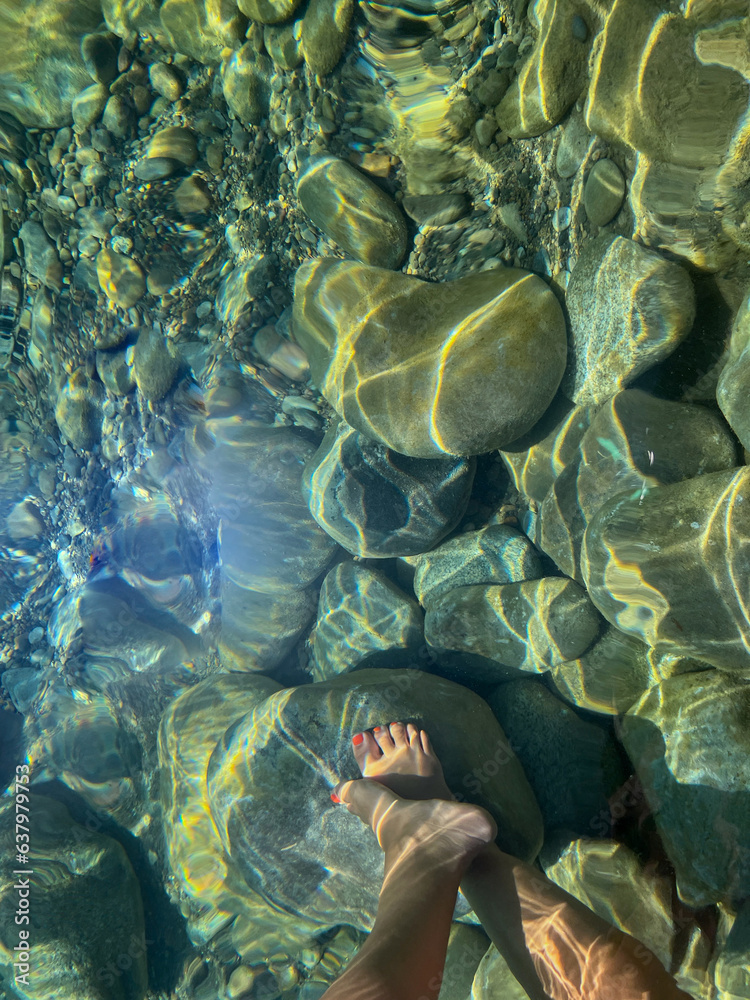 woman's feet in crystal clear river water with round stones and ...