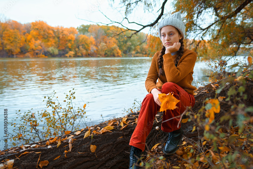 a young teenage girl posing in an autumn forest, sitting on a tree by ...