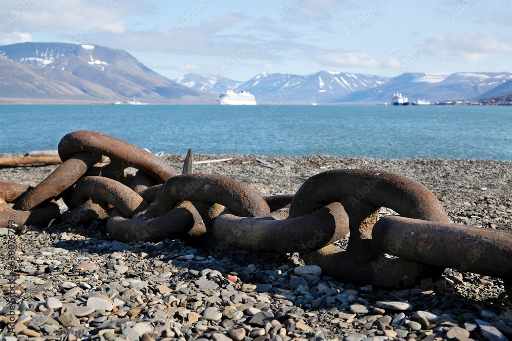 A rusty metal chain ship lies on the shore of the fjord in Longyearbyen ...