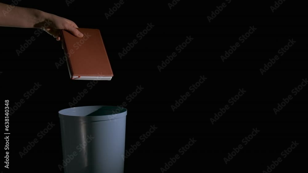 Throwing book away in bin. Somebody throw the book into the plastic bin ...