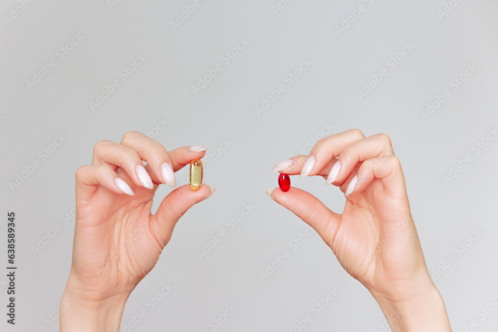 female hands holding yellow and red gel capsules with their fingers ...