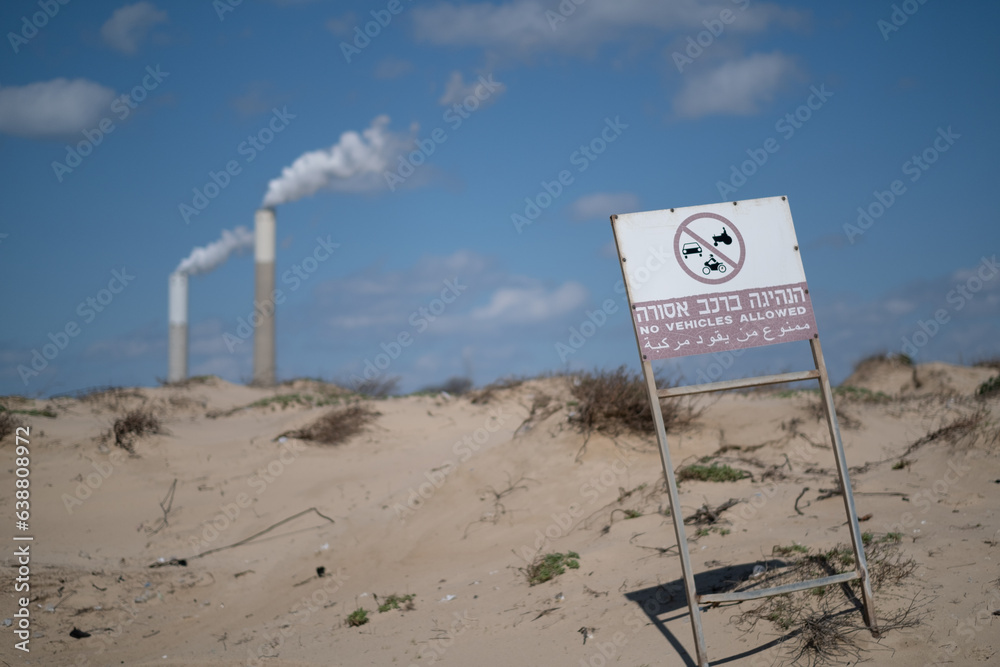 A warning sign banning vehicle access is posted on a dune, with two ...