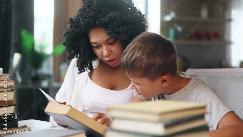 Cute primary school boy kid studying with his mother reading book at ...