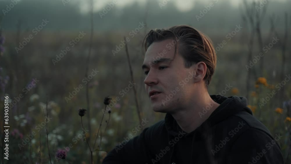 Melancholic serious man musician singing song sitting on field among ...