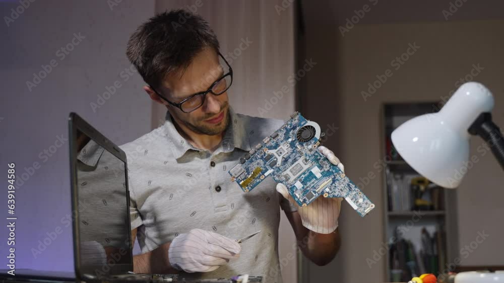 Man in glasses and gloves examines laptop motherboard for defects and ...