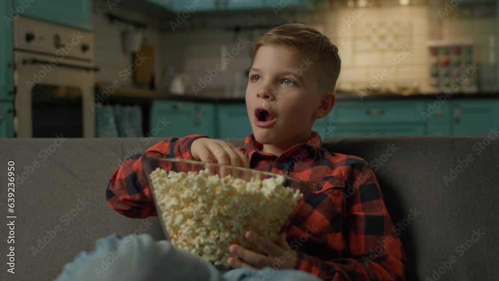 Boy Eating Popcorn Watching TV. Child enjoys snack sitting on sofa at ...