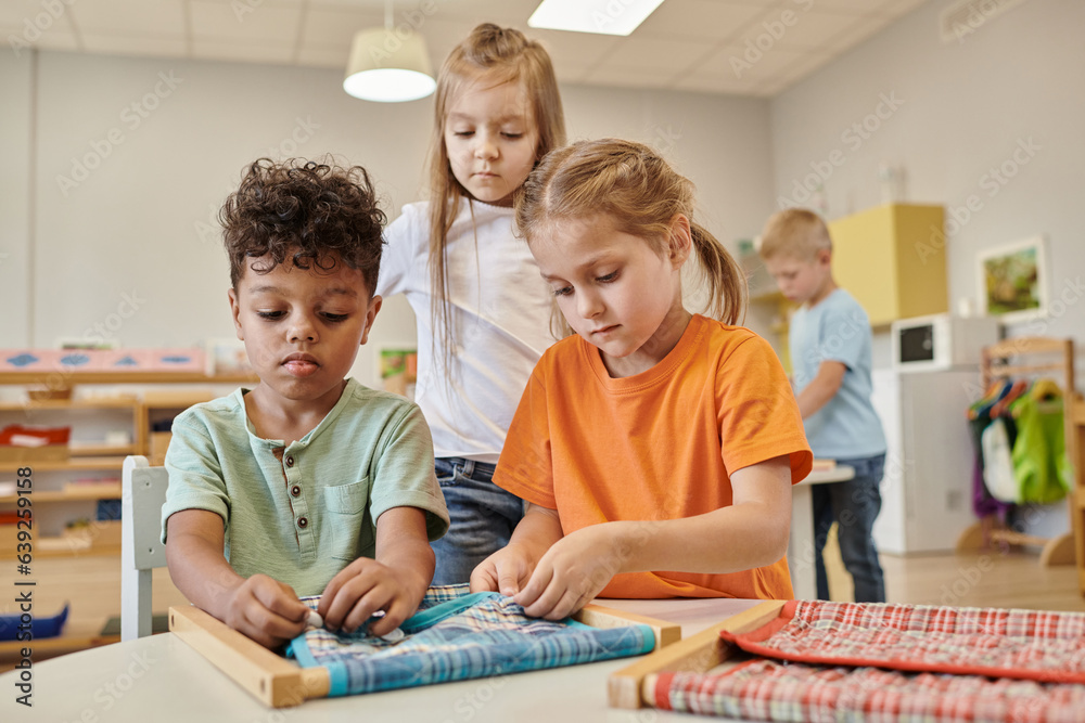 interracial kids playing with cloth and buttons on frame in class of ...
