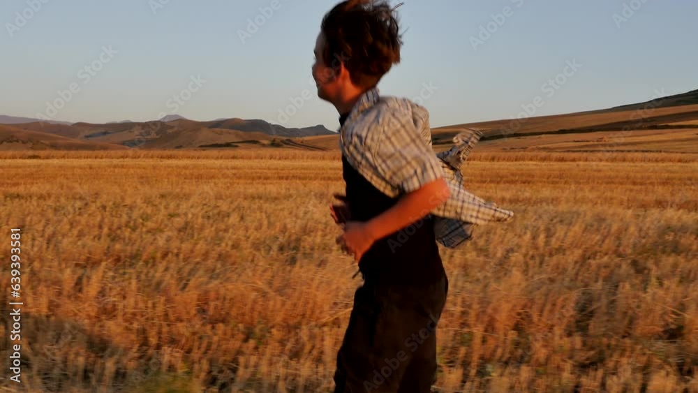 A teenage child running across a field at sunset after the harvest. A ...