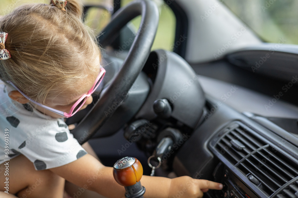 A small child plays with the buttons in the car while sitting behind ...