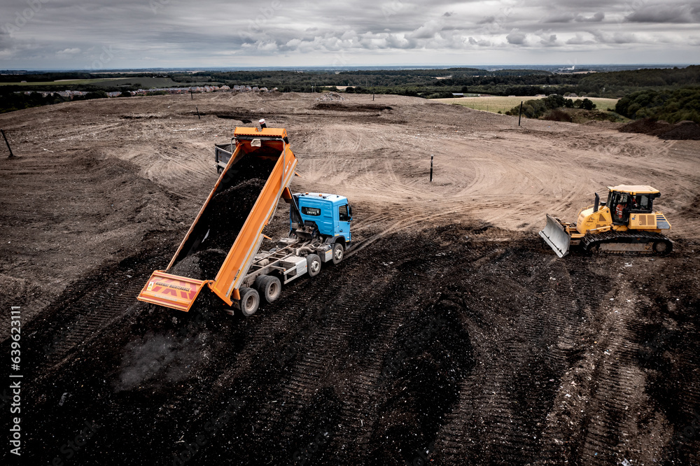 Aerial view of a tipper truck with raised trailer unloading landfill ...