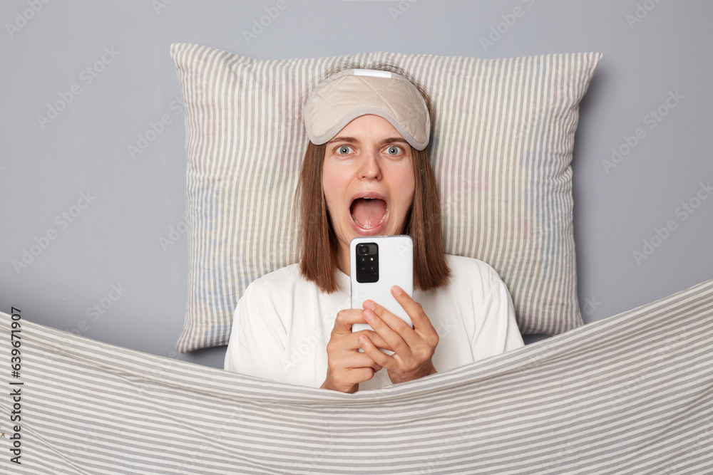 Shocked scared young woman wearing white T-shirt and sleep eye mask ...