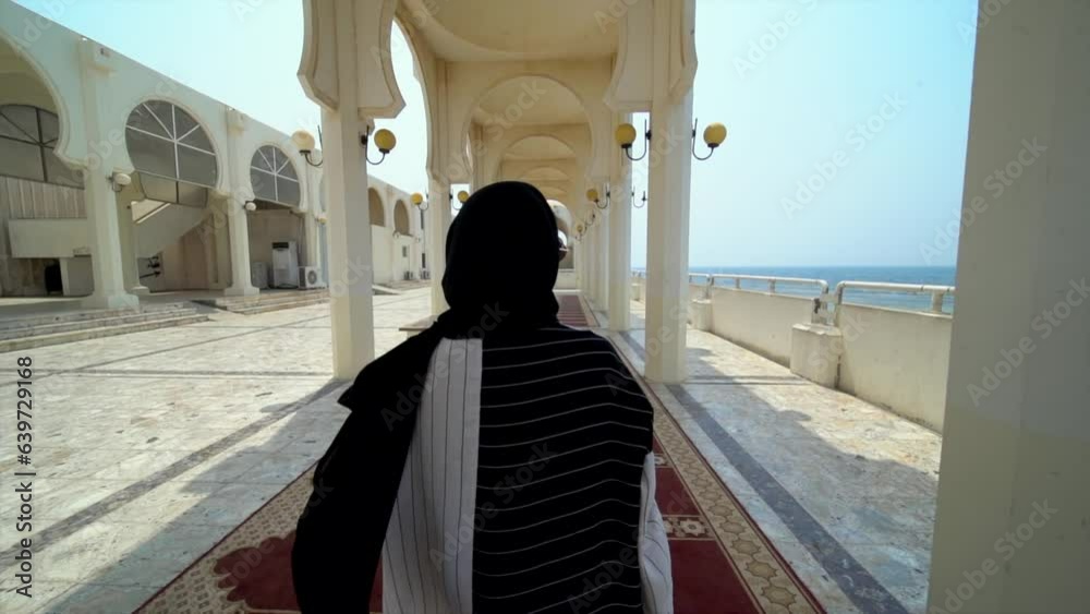 A woman in black and white arabic clothing walking on a carpet in a ...