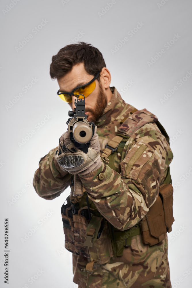 Serious bearded male sniper aiming, by pointing machine gun to camera ...
