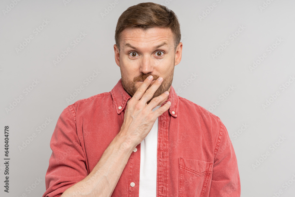 Shy amazed confused man covering mouth with hand looking at camera ...