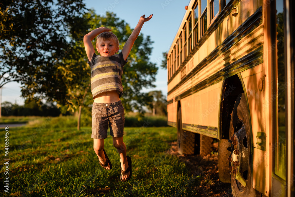 Young child jumping for joy next to school bus during back to sc Stock ...