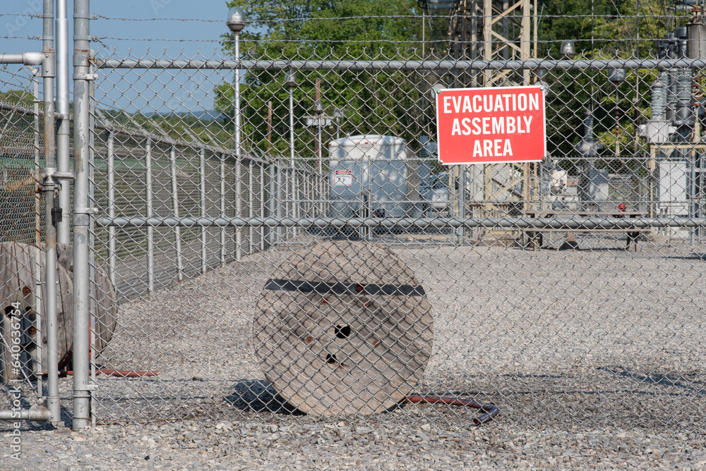Red and white, Evacuation assembly area sign hanging on a chain linked ...