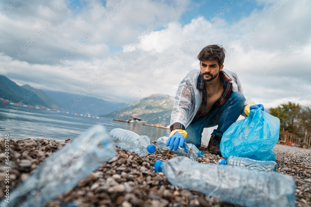 Confident handsome man cleaning up the beach from plastic waste ...