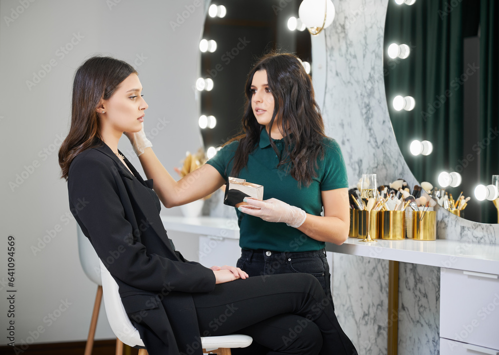 Stylish woman sitting on stool at dressing table while beauty ...