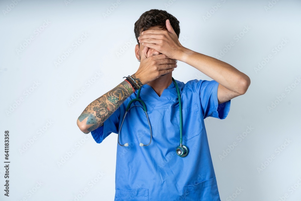 young caucasian doctor man wearing blue medical uniform Covering eyes ...