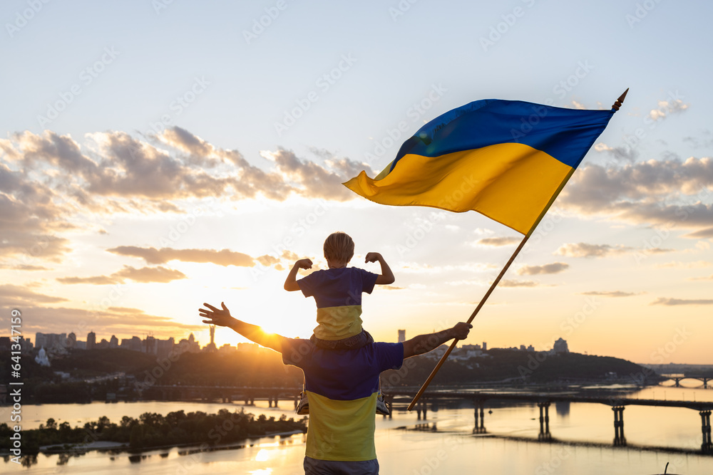 dad with son, who sits on shoulders, with large flag of Ukraine on roof ...