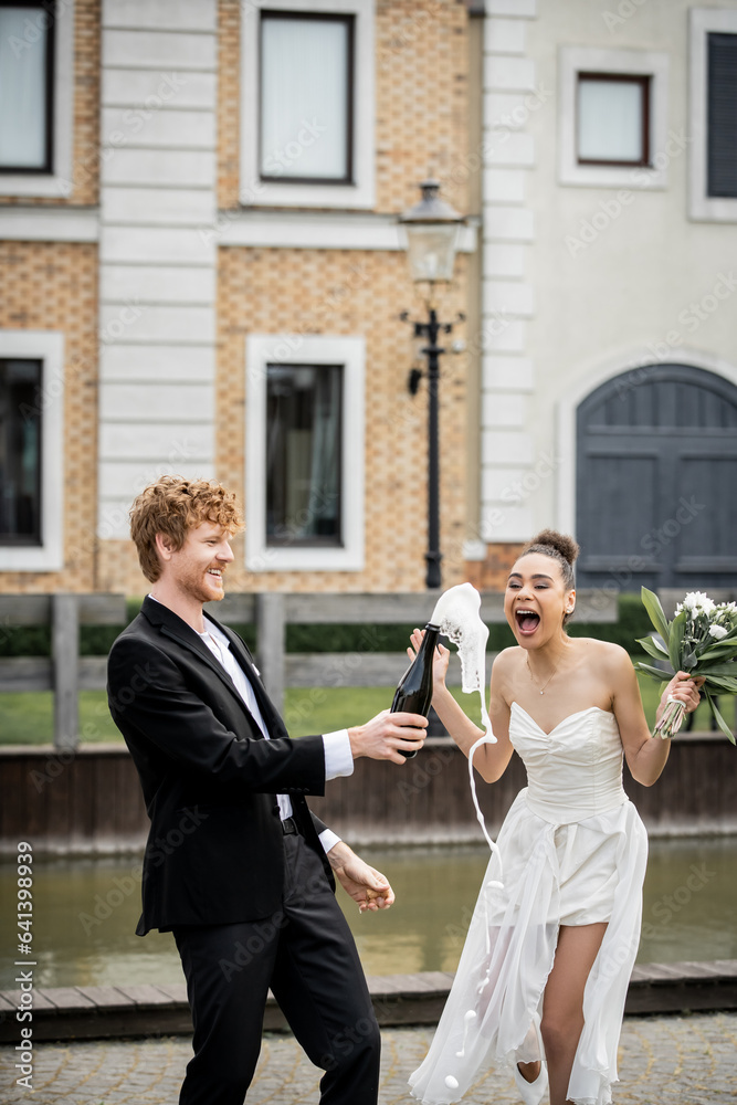 excited african american bride near groom with champagne pouring from ...
