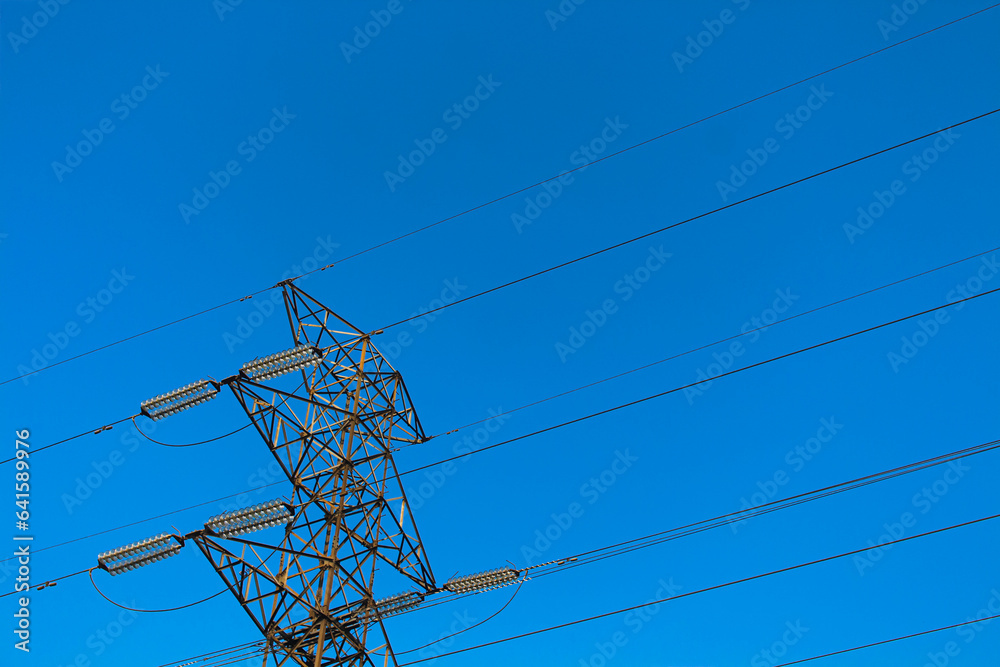 Electric towers and cables that stretch against a bright blue sky and ...