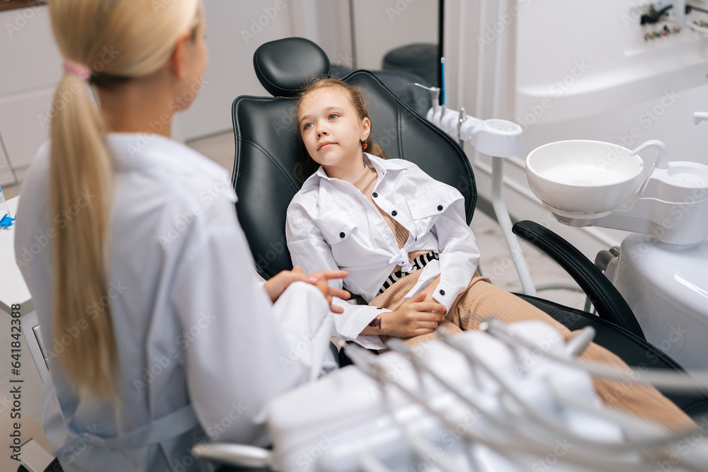 Back view of cute little girl sitting on dental chair and complaining ...