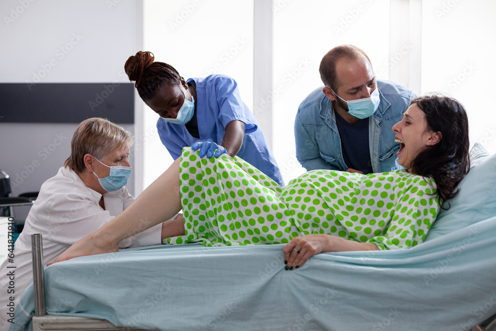 Pregnant woman lying in bed giving birth to baby in hospital ward while ...