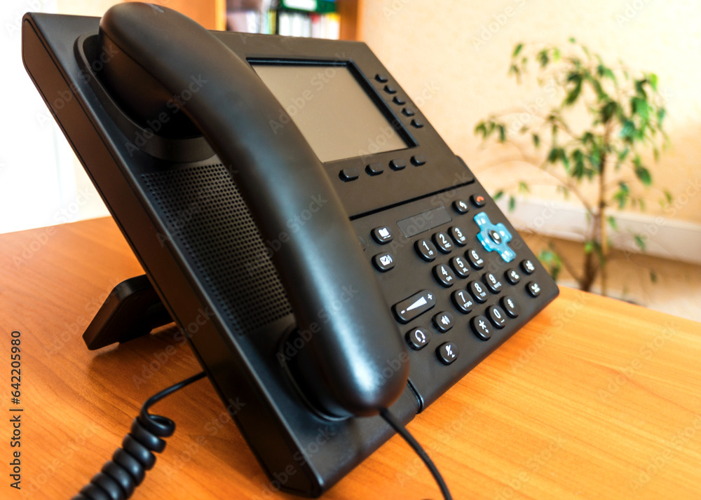 The black desktop push-button telephone. IP phone on desk in office ...